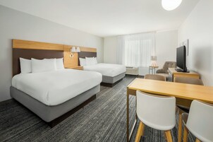 Quarto de hotel com duas camas, uma escrivaninha, uma cadeira, uma televisão e uma janela com cortinas.