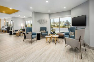 Uma área de estar espaçosa e moderna, com assentos confortáveis, uma TV de tela plana e janelas amplas que oferecem vista para o exterior.