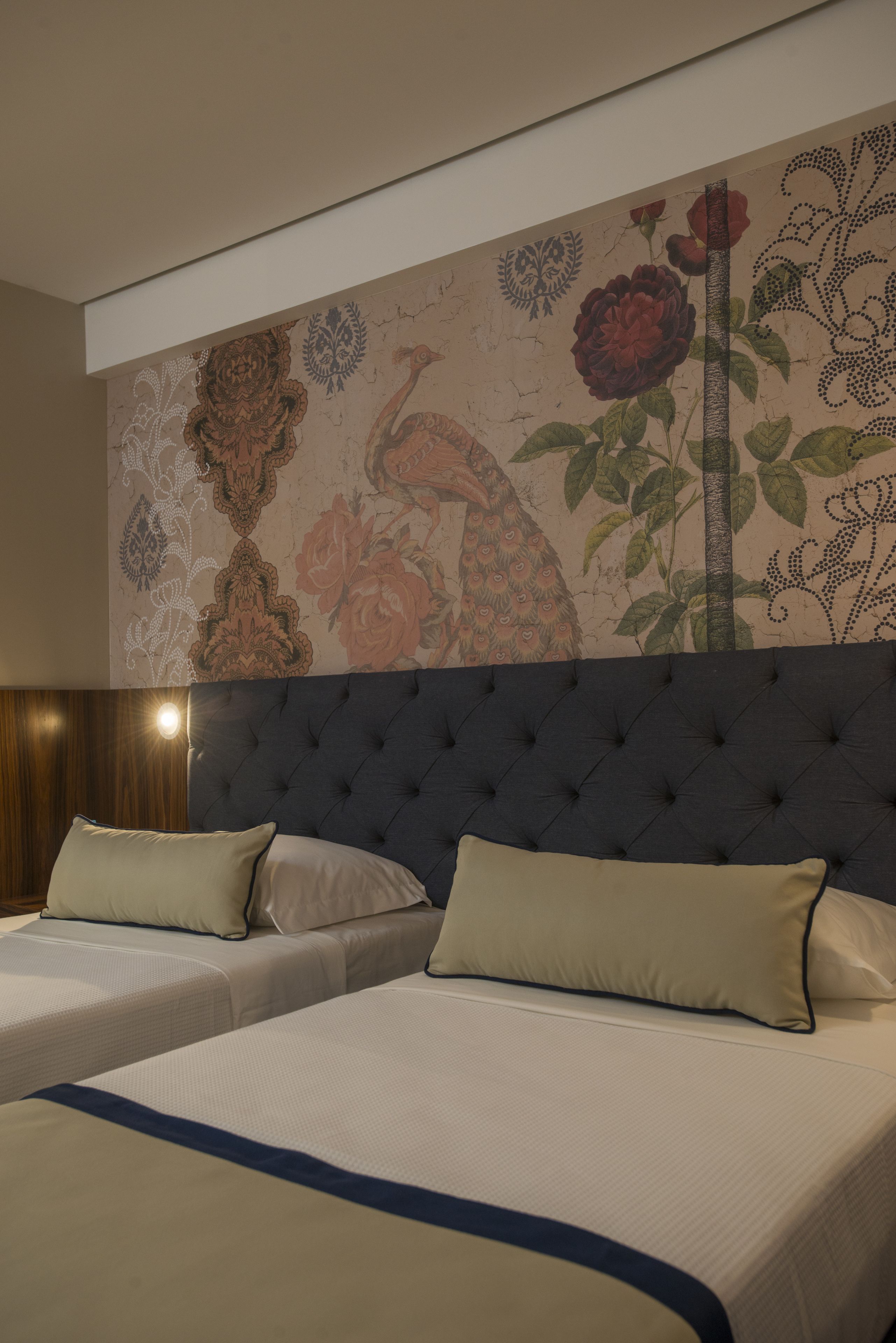Quarto de hotel com duas camas, cabeceira escura e painel floral na parede.