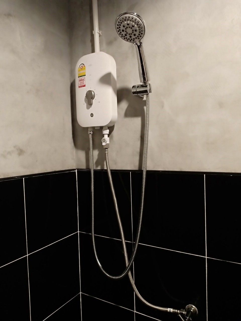 Casa de banho com chuveiro branco, paredes revestidas a azulejos pretos e cano de água visível.