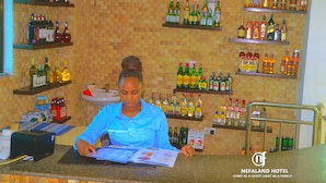 Um bar de hotel com prateleiras cheias de garrafas de bebidas e uma mulher trabalhando no balcão.