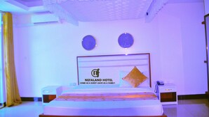 Quarto de hotel com uma cama, duas mesas de cabeceira, um criado-mudo, uma luminária e um letreiro fixado na parede.