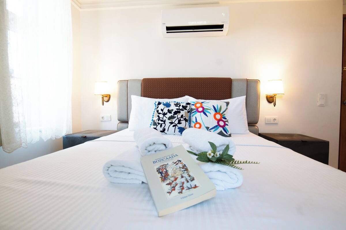 Quarto de hotel com uma cama bem arrumada, um livro intitulado 'BOZCAÑA' e uma almofada decorativa.