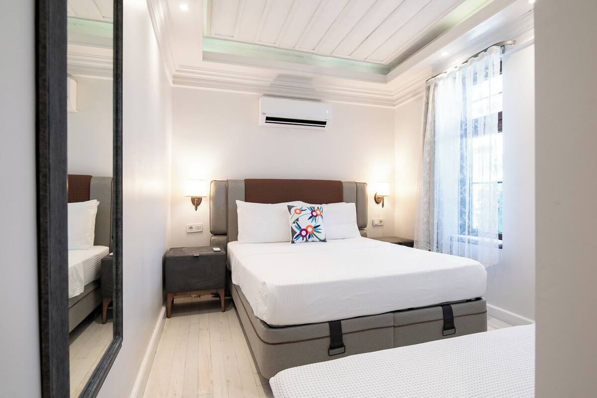 Quarto de hotel com cama, mesas de cabeceira, espelho, ar condicionado e janela com cortinas.