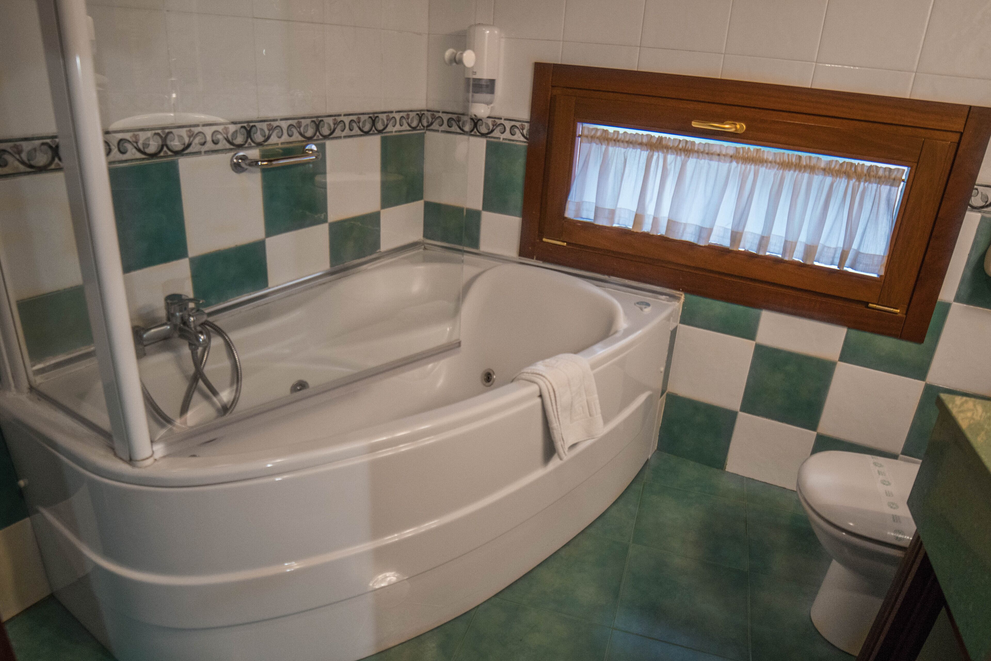Um banheiro com banheira, vaso sanitário e uma janela com cortinas.