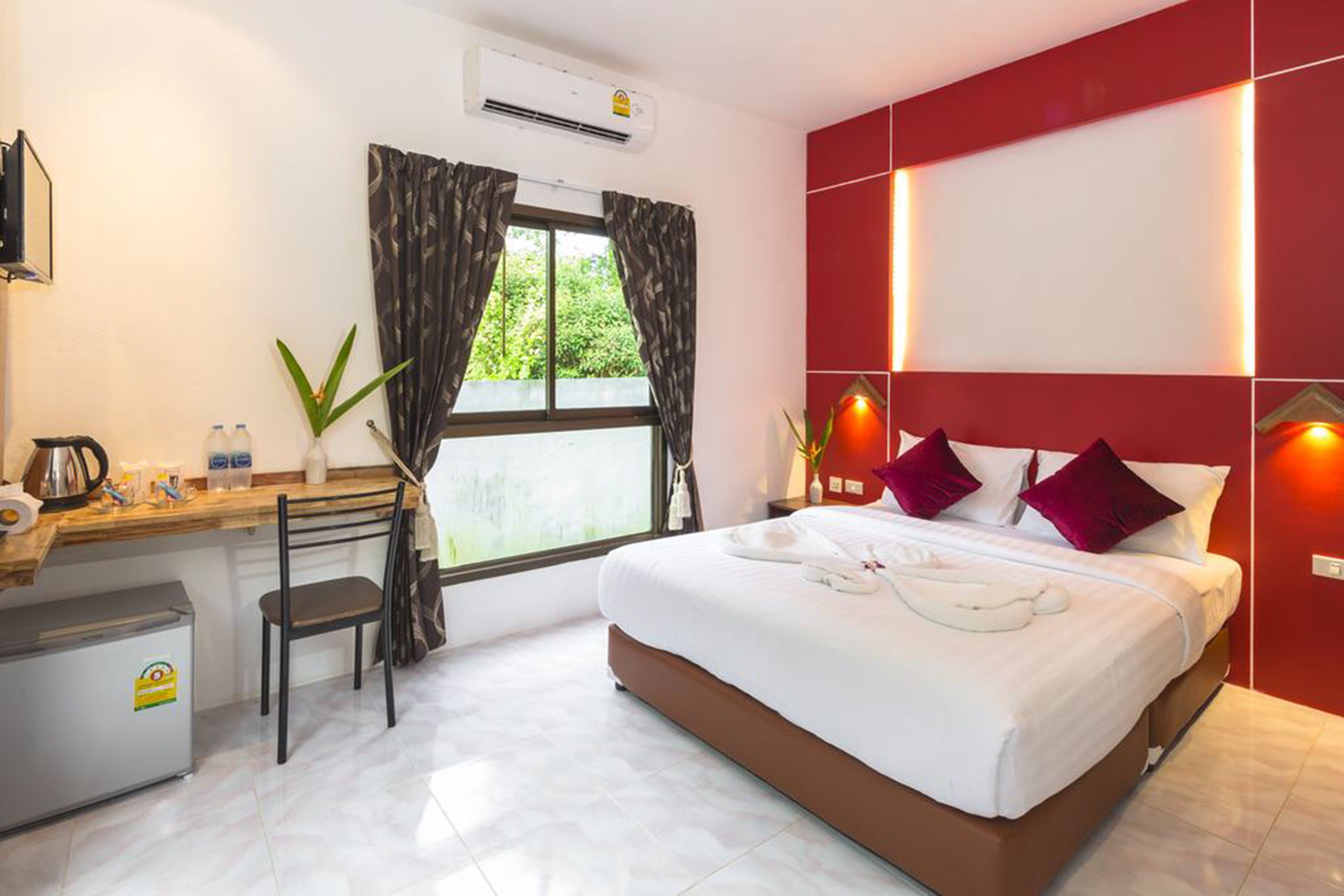 Quarto de hotel com cama, escrivaninha, cadeira, mini-geladeira e janela com cortinas.