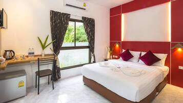 Quarto de hotel com cama, escrivaninha, cadeira, mini-geladeira e janela com cortinas.
