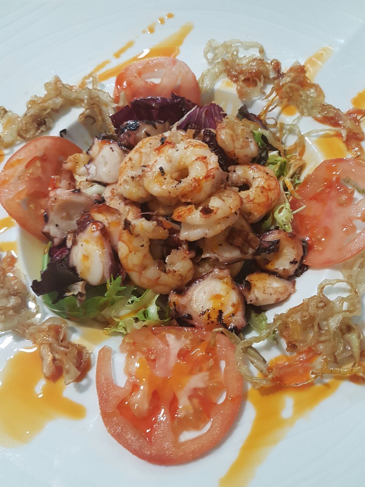 Um prato de camarões grelhados com legumes e um fio de molho.