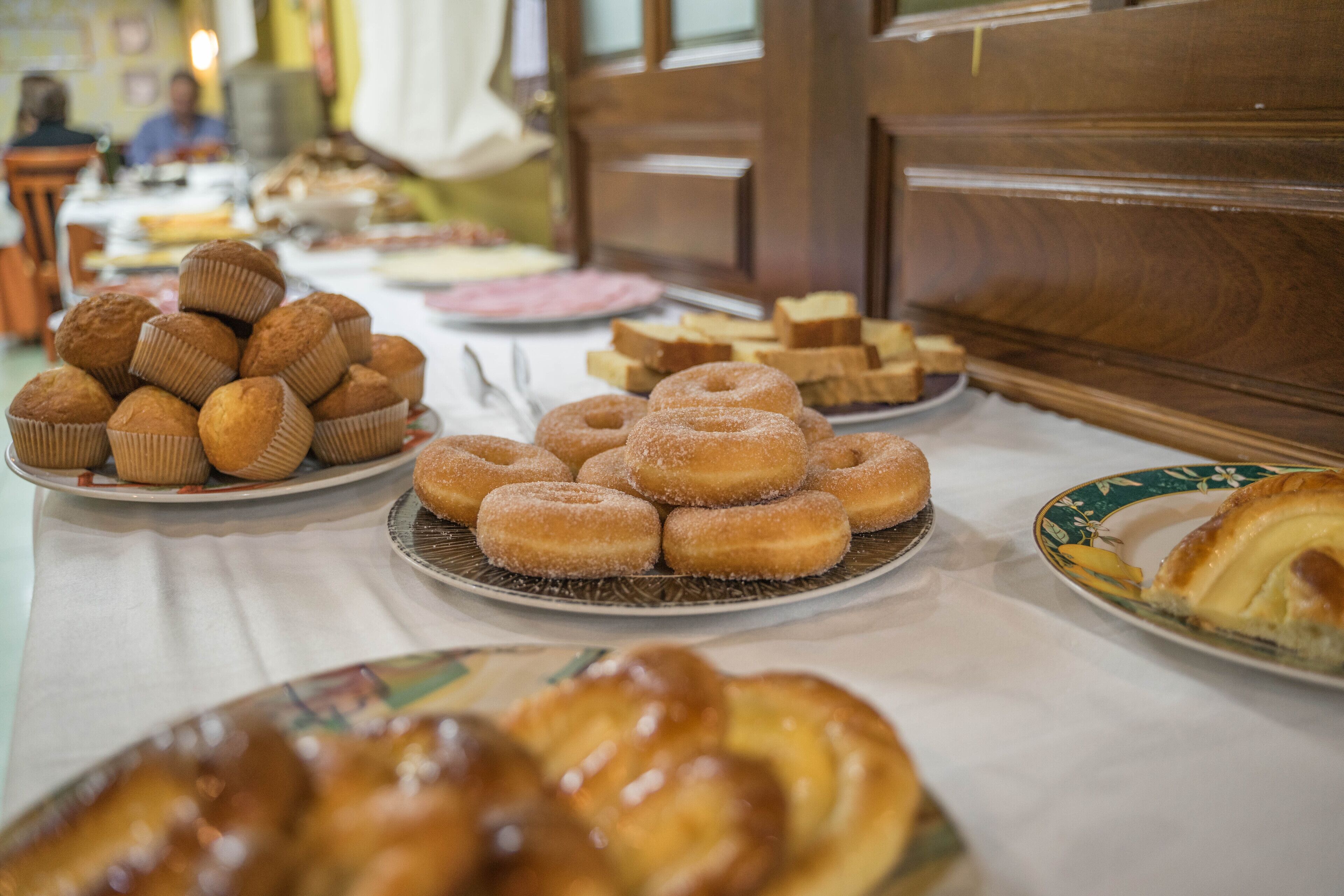 Mesa de buffet com diversos produtos de panificação, incluindo muffins, donuts e doces.