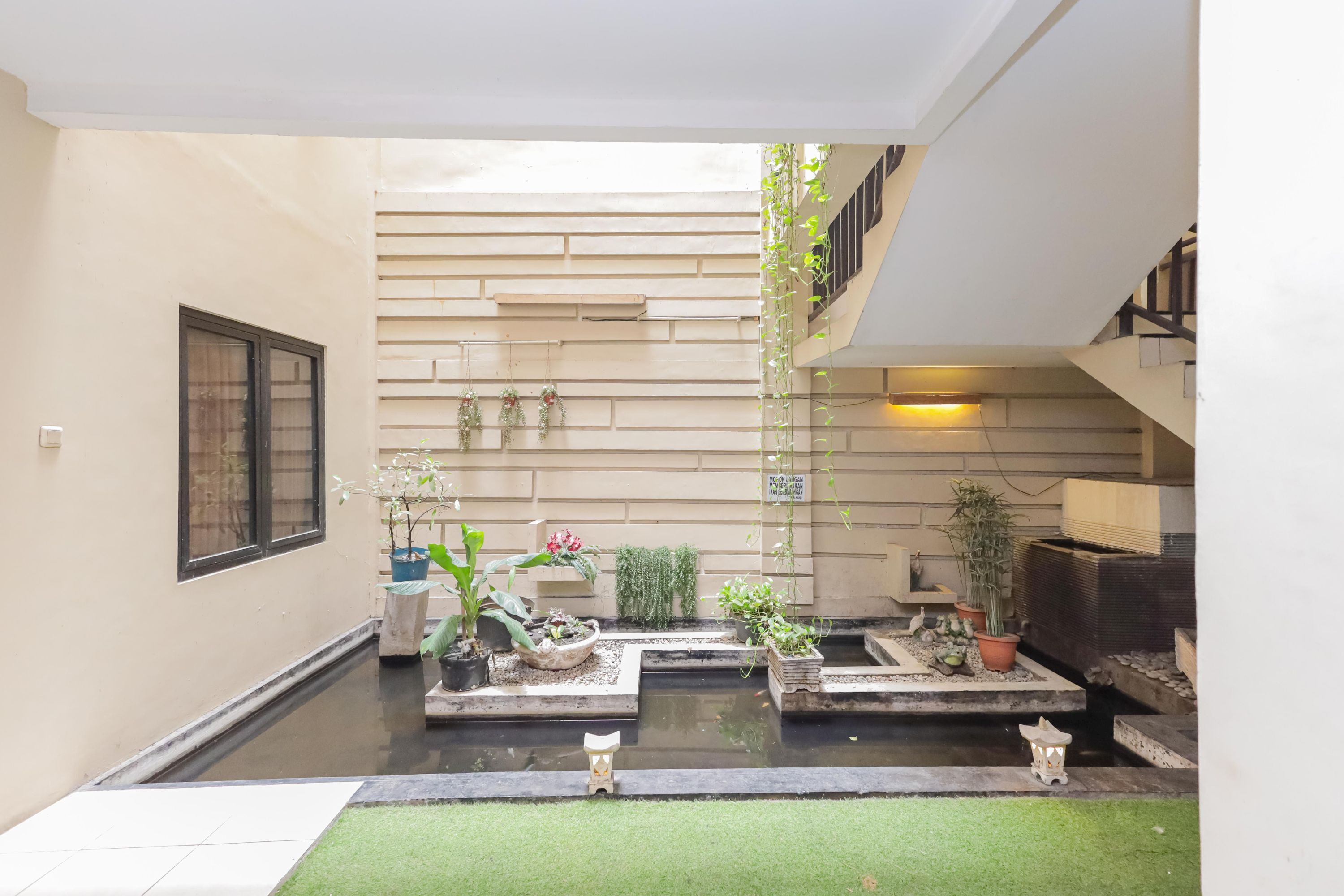Um jardim interno moderno com um elemento de água, plantas em vasos e um pequeno candeeiro.