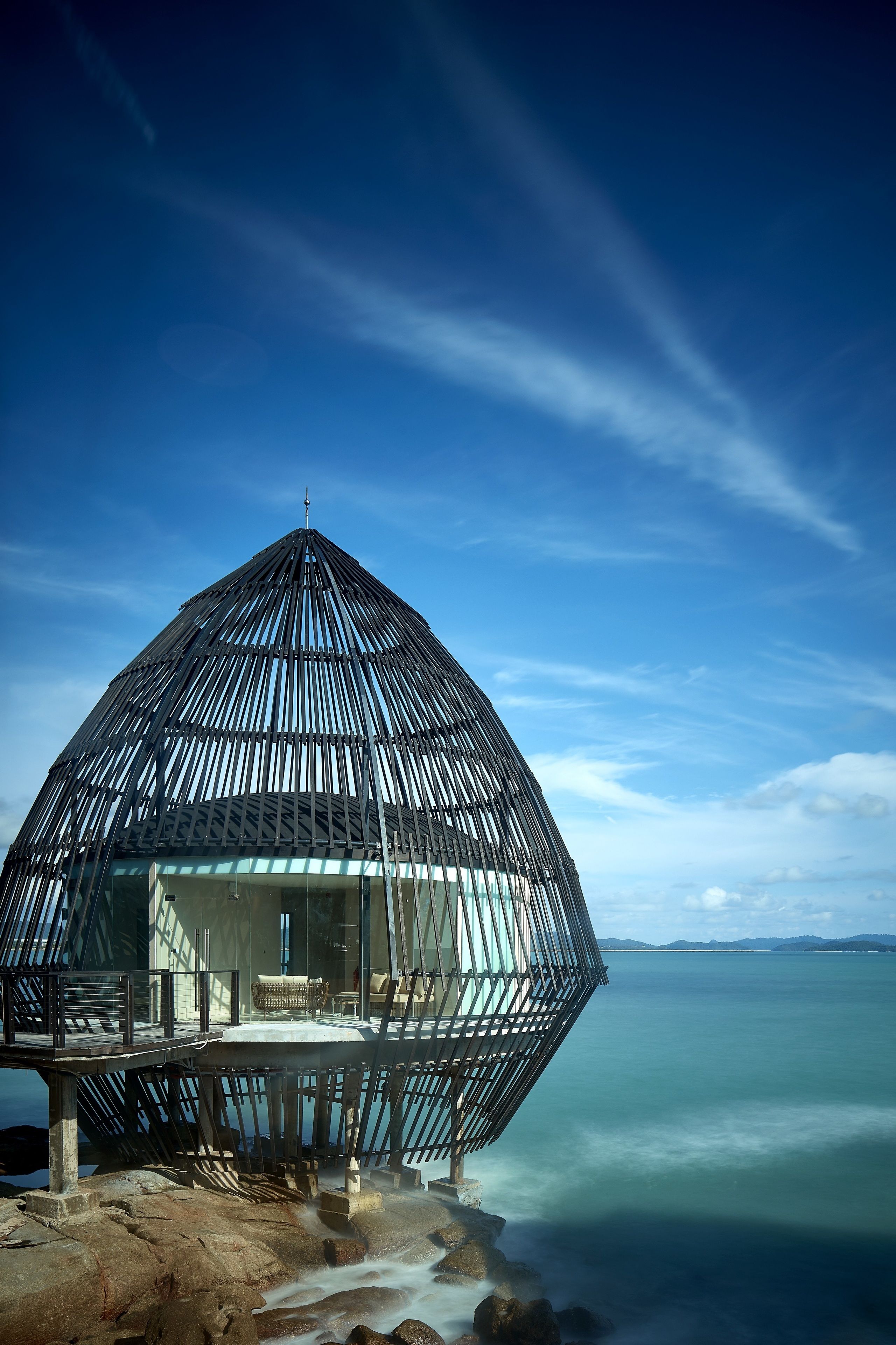 Uma estrutura em forma de cúpula geodésica com piso de vidro, com vista para um corpo de água.