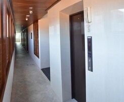 Um corredor com teto de madeira, chão de azulejos e porta com telefone e painel de comando de elevador.