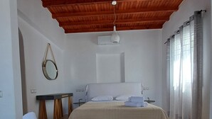 Quarto de hotel com duas camas, teto de madeira, espelho redondo, mesa pequena e janela com cortinas.