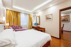Quarto de hotel com uma cama grande, uma escrivaninha com um computador, uma cadeira e uma porta que dá para outro quarto.