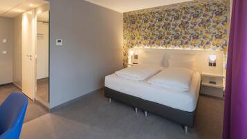 Quarto de hotel com uma cama, mesas de cabeceira, uma cadeira e parede com padrão.