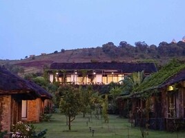 Um hotel com um edifício moderno e cabanas tradicionais, rodeado por uma área gramada e árvores.