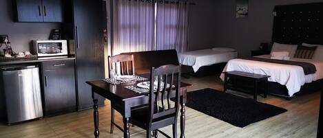 Quarto de hotel compacto com cozinha compacta, área de refeições, duas camas de solteiro e uma pequena escrivaninha.