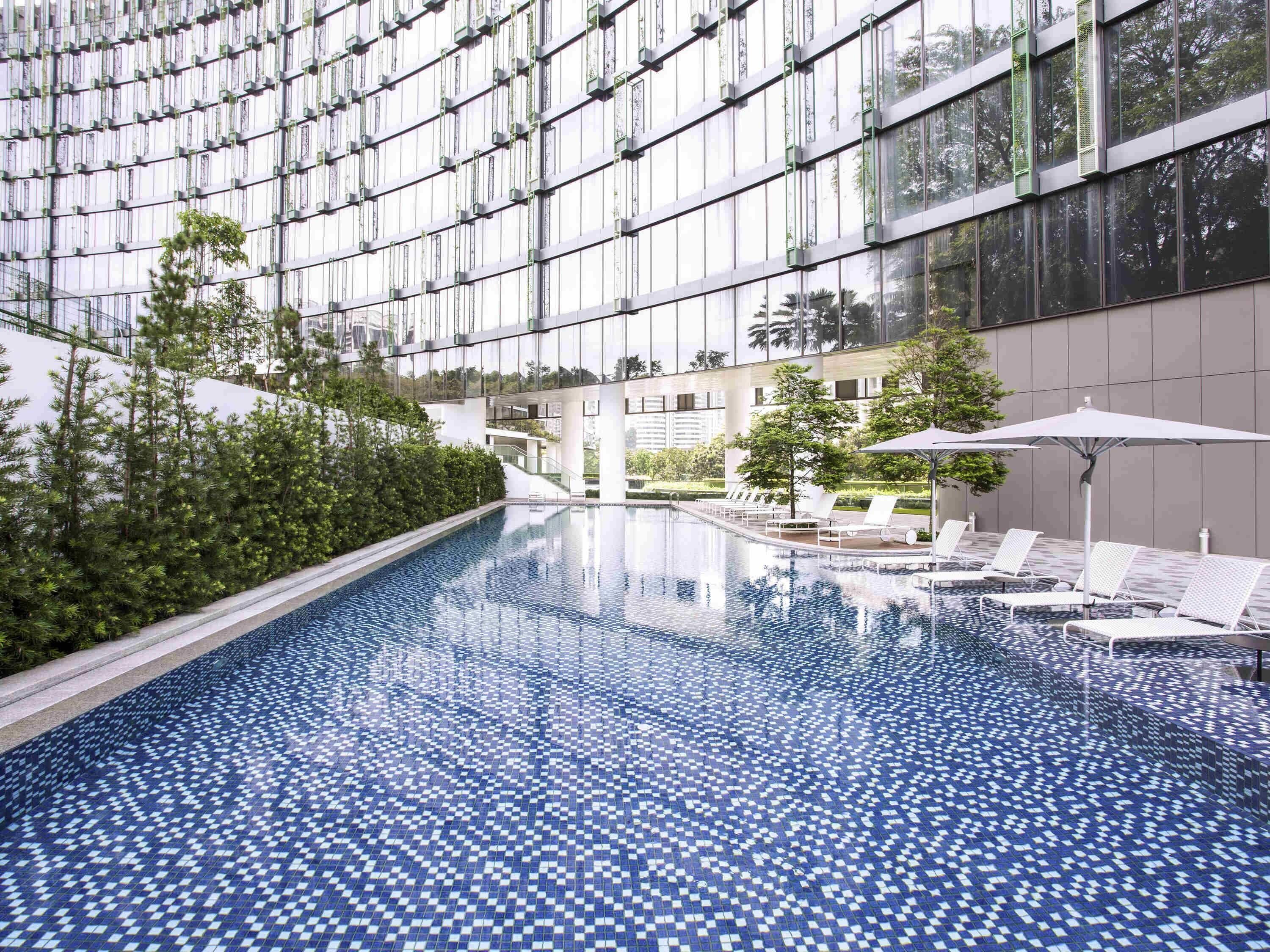 Piscina interior moderna com chão de azulejos, rodeada por plantas e espreguiçadeiras.