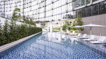 Piscina interior moderna com chão de azulejos, rodeada por plantas e espreguiçadeiras.