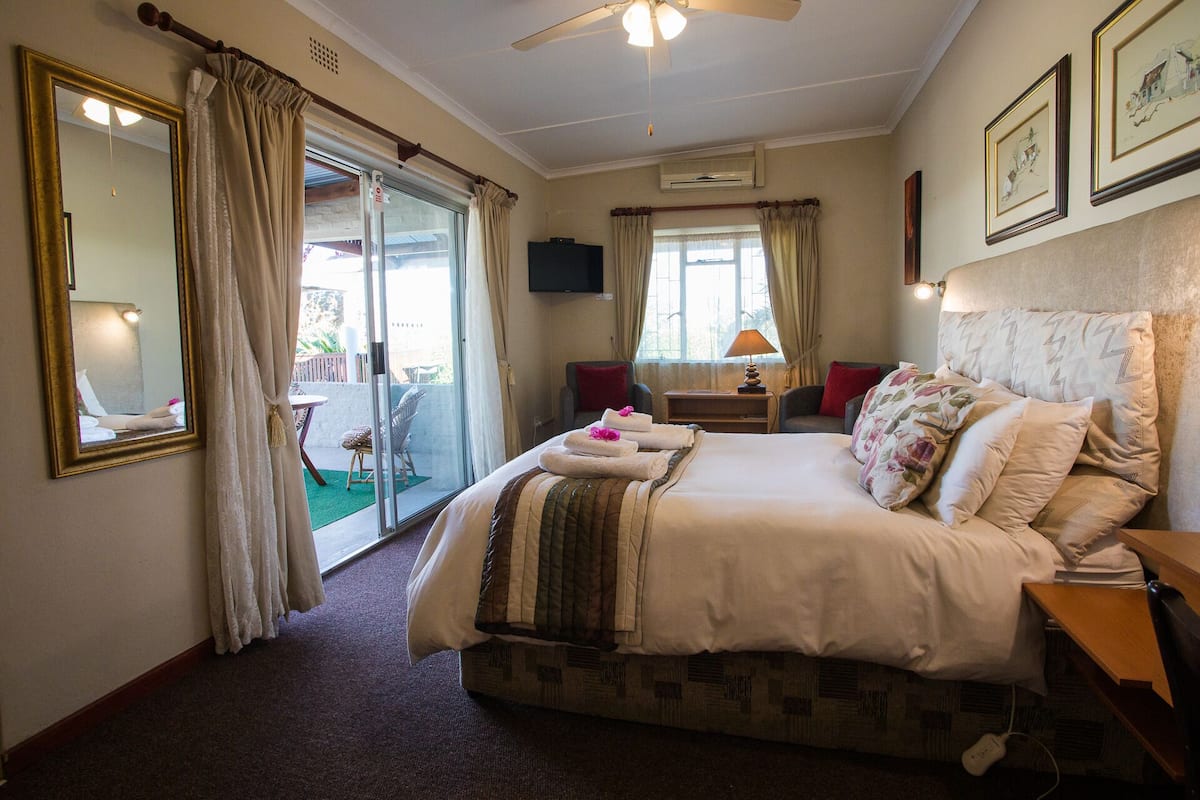 Quarto de hotel com cama, escrivaninha, cadeira, televisão e varanda com mesa e cadeiras.