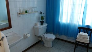 Casa de banho com sanita, lavatório e uma cadeira com toalhas.