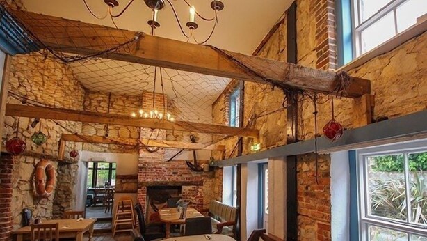 Um interior rústico com paredes de tijolo aparente, vigas de madeira e uma grande mesa de jantar com cadeiras.