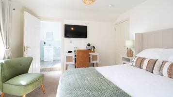 Quarto de hotel com uma cama, uma secretária com cadeira, televisão e casa de banho visível através de uma porta aberta.