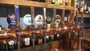 Um balcão de bar com várias torneiras de cerveja, incluindo marcas como Foster, IPA e Moretti.