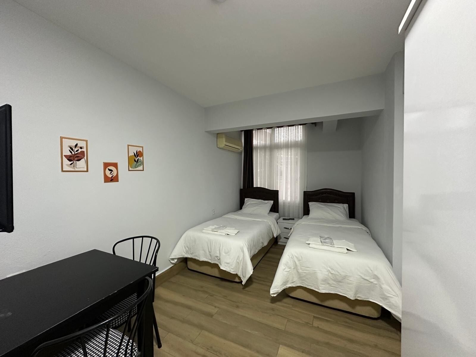 Quarto de hotel com duas camas de solteiro, uma escrivaninha e uma cadeira. Há duas imagens emolduradas na parede.