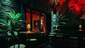 Uma área de estar ao ar livre com iluminação suave, mesas e cadeiras, cercada por vegetação exuberante e plantas tropicais.