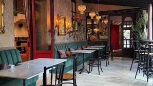 Interior de restaurante com assentos estofados verdes, mesas de mármore e cadeiras pretas.