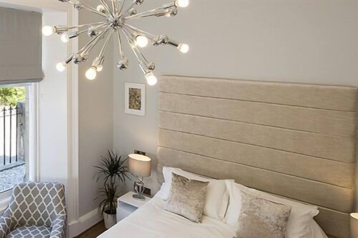 Quarto com uma cama grande, um candelabro moderno, uma mesa de cabeceira com abajur e uma cadeira.