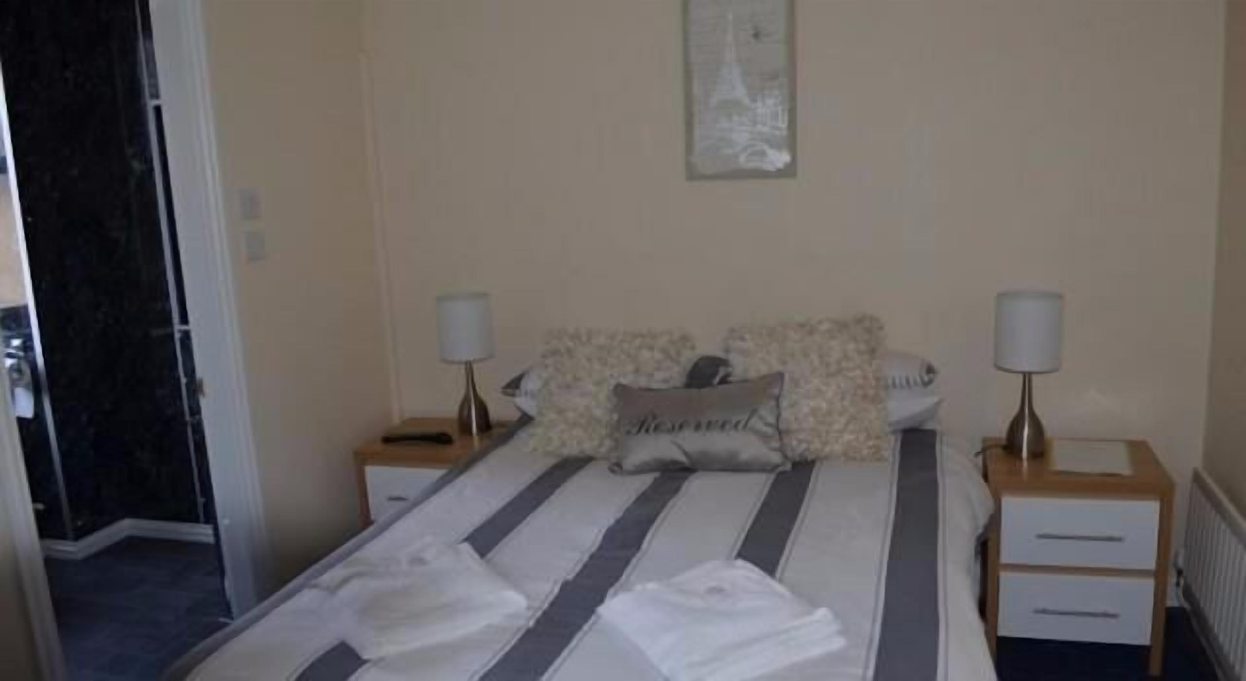 Quarto de hotel com cama, duas mesas de cabeceira, duas luminárias, um travesseiro e um quadro na parede.