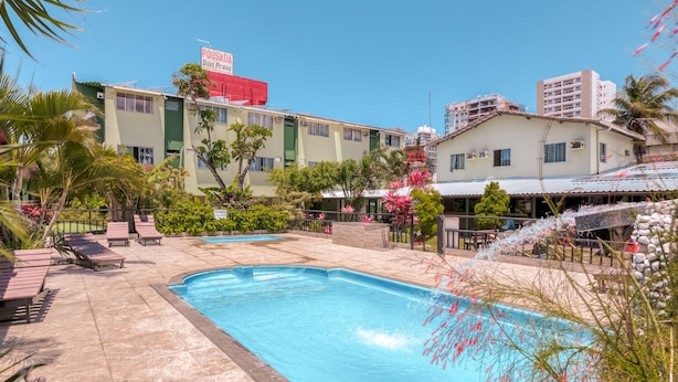 Piscina com espreguiçadeiras, rodeada por vegetação e edifícios.