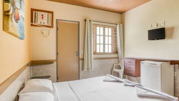 Quarto de hotel com cama, uma secretária pequena, televisão e janela com cortinas.