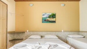 Quarto de hotel com duas camas, um quadro de uma paisagem de praia e um revestimento de azulejos.