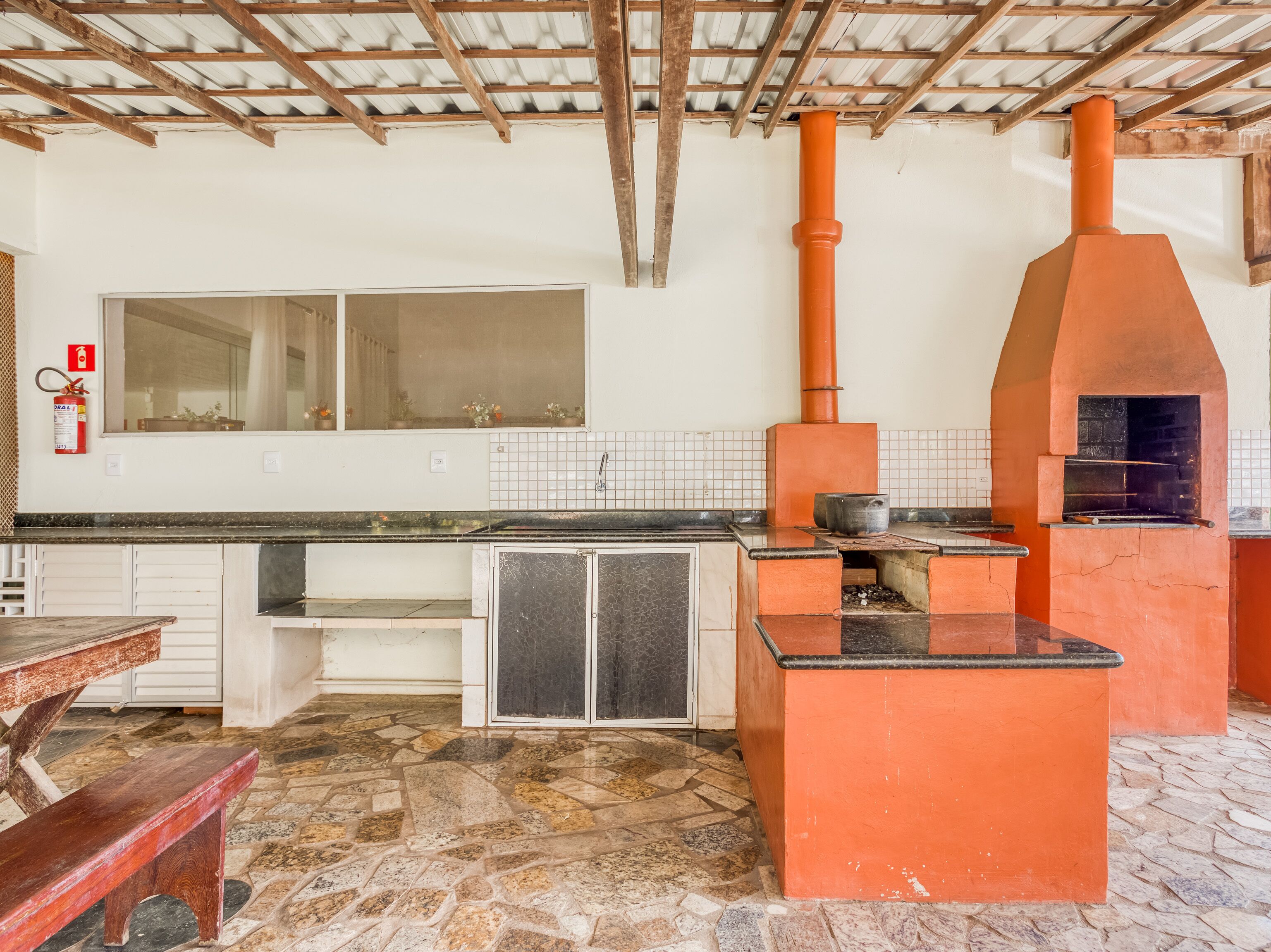 Uma cozinha com piso de pedra, vigas de madeira, um forno grande e um extintor de incêndio.