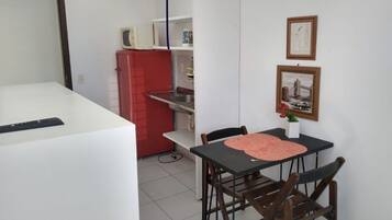 Um espaço compacto com cozinha americana, área de refeições com mesa e cadeiras, e uma pequena geladeira.