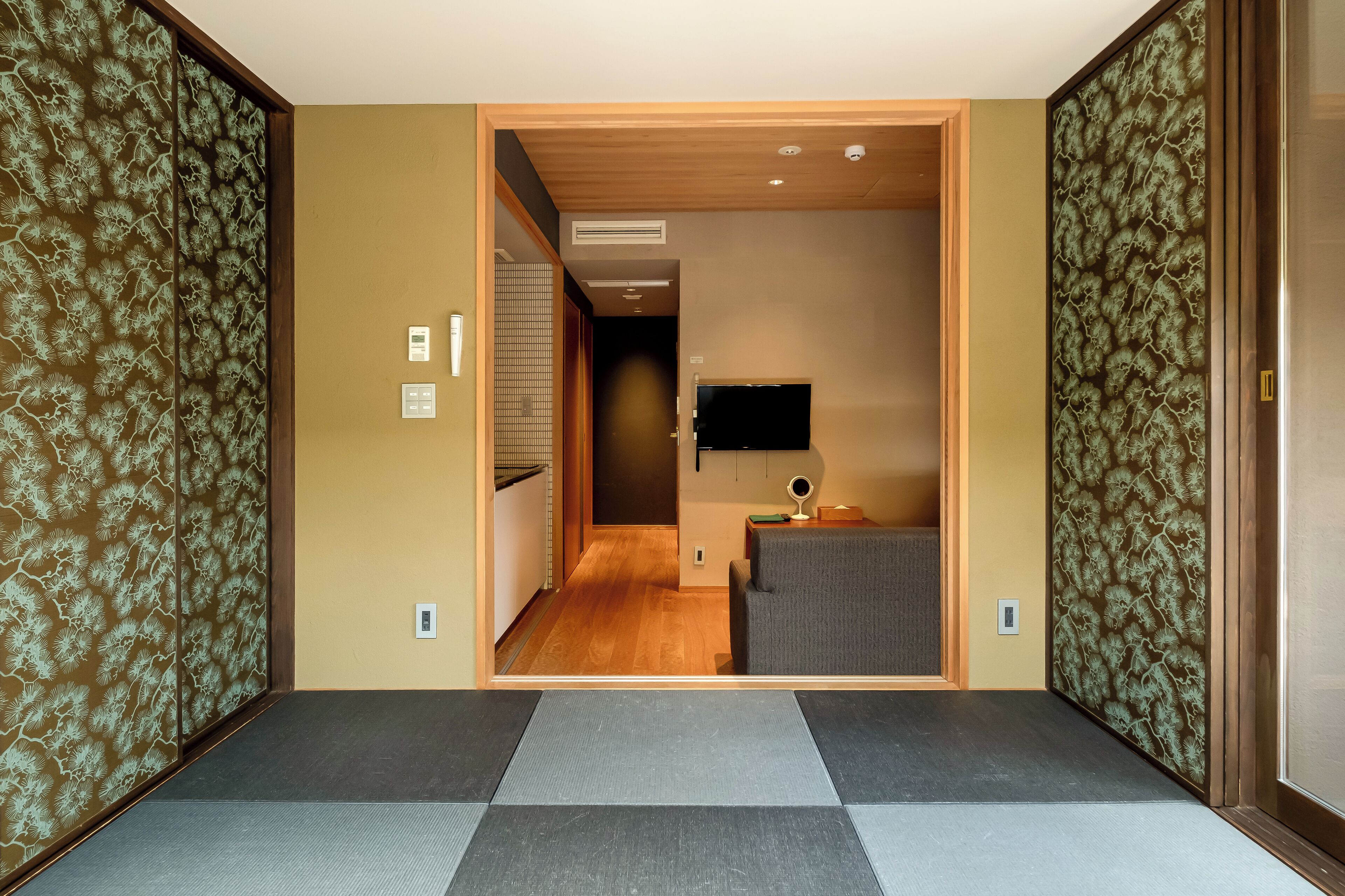 Um quarto japonês tradicional, com tatames, uma porta deslizante, uma televisão e uma pequena mesa.
