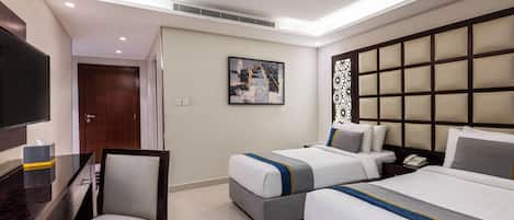Quarto de hotel com duas camas, uma escrivaninha, uma cadeira, uma TV e um quadro na parede.