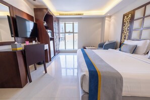 Quarto de hotel com uma cama, uma escrivaninha com televisão e uma janela grande.