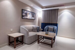 Uma sala de estar moderna com um sofá cinzento, uma poltrona azul, uma mesinha e um quadro na parede.
