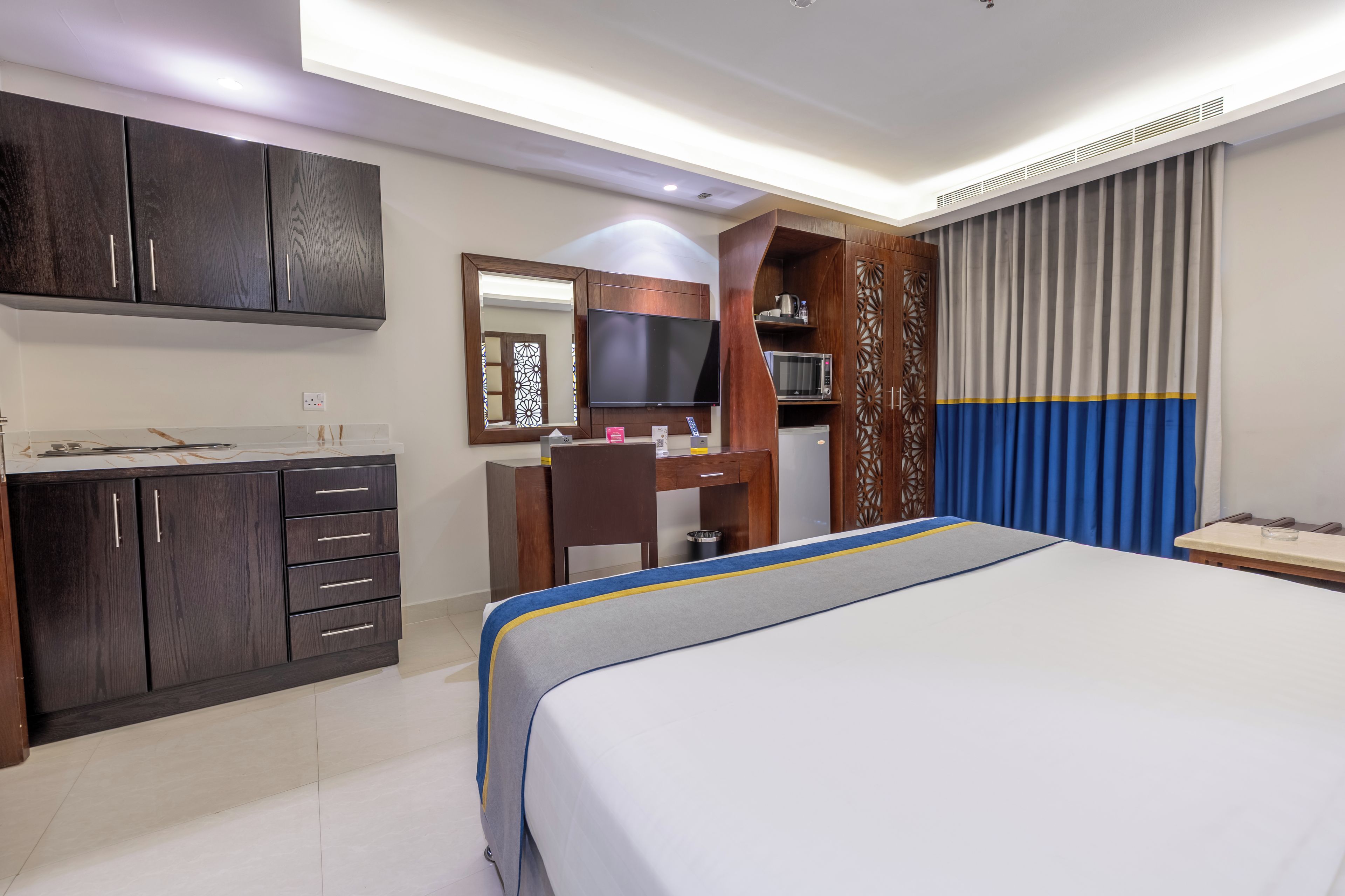 Quarto de hotel com cama, escrivaninha, televisão e guarda-roupa.