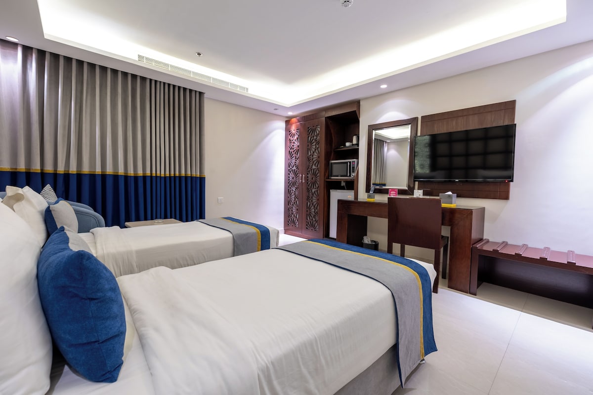 Quarto de hotel com duas camas, uma escrivaninha, televisão de tela plana e micro-ondas.