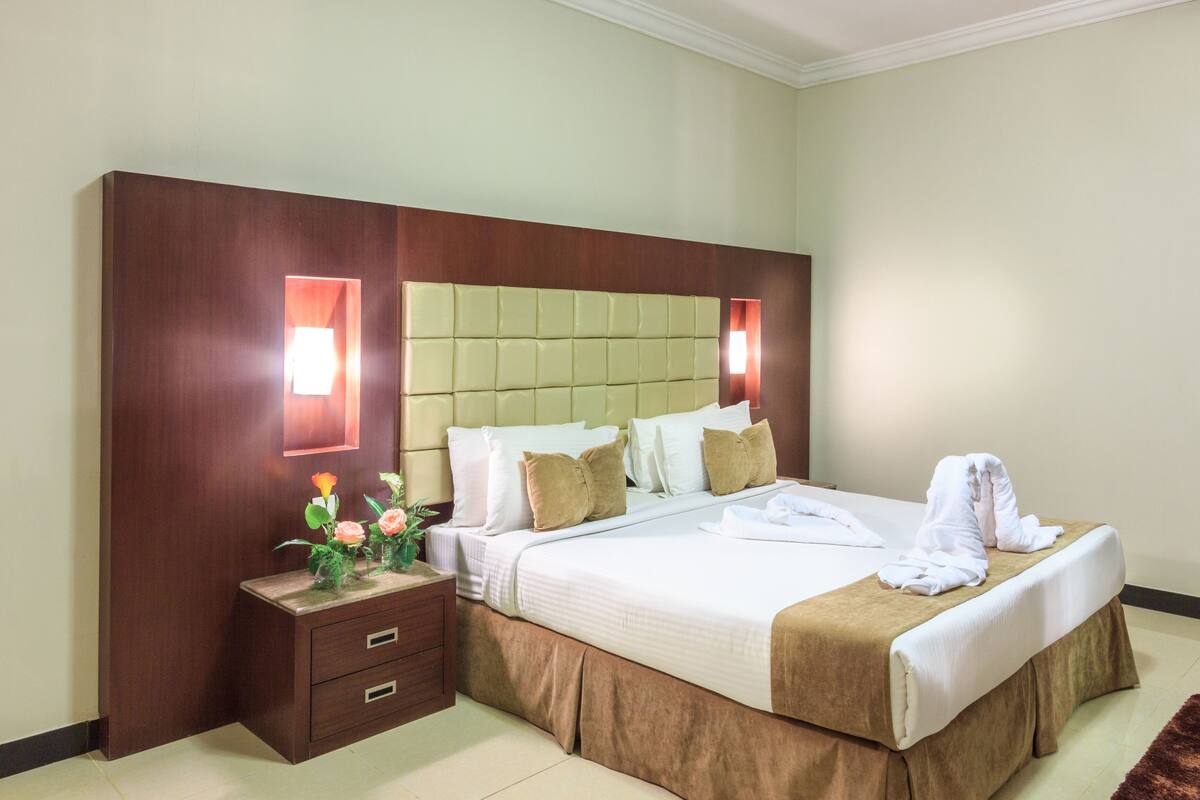 Quarto de hotel com uma cama grande, uma mesa de cabeceira com gavetas e duas luminárias fixadas na parede.