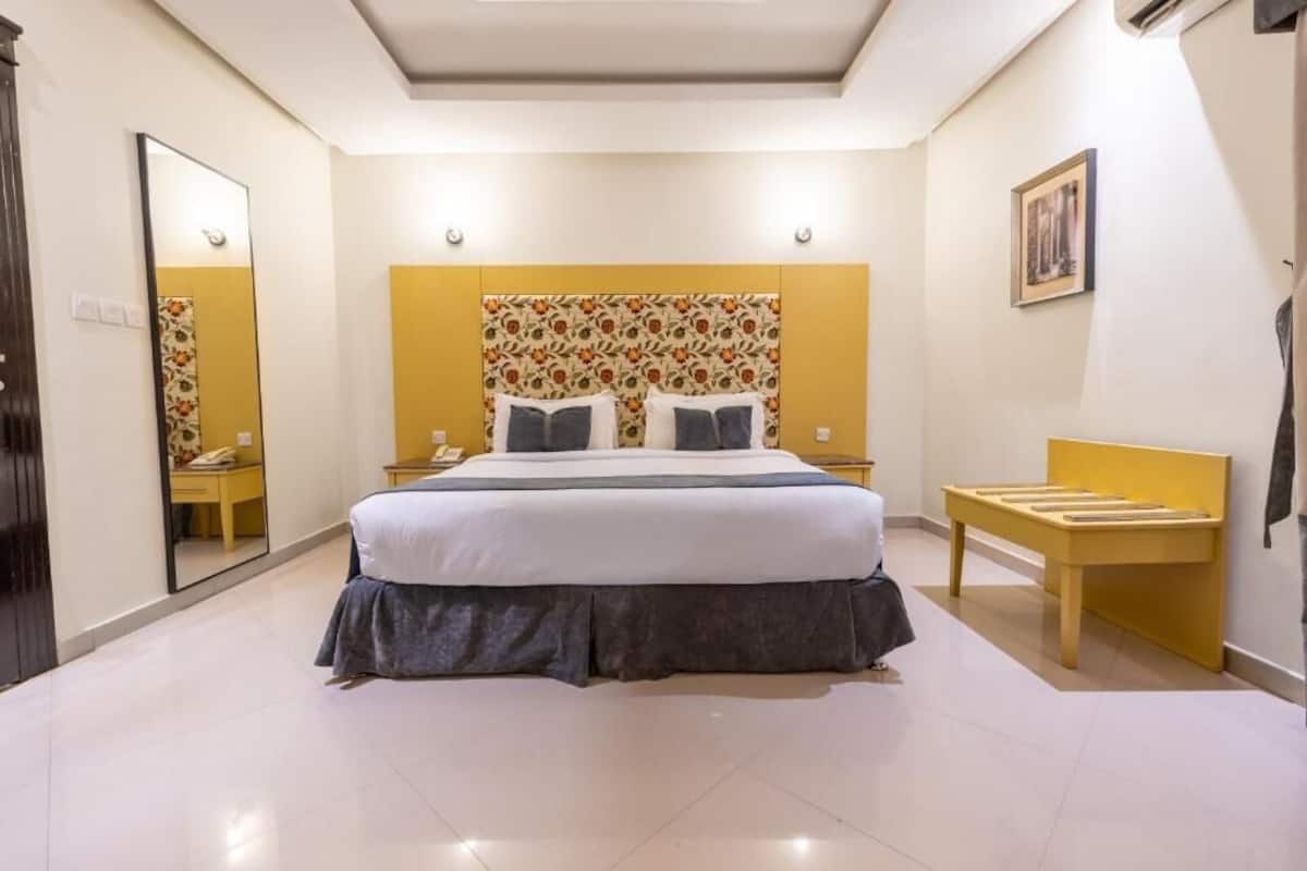 Quarto com uma cama grande, mesas de cabeceira, um banco, um espelho e um quadro pendurado na parede.