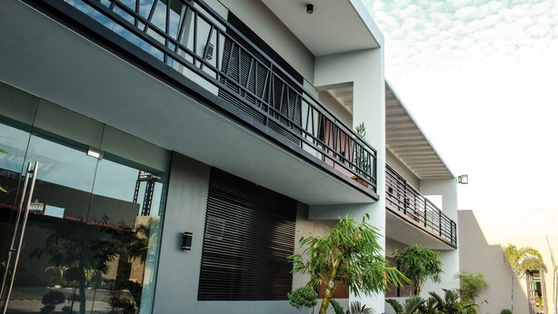 Um edifício moderno com fachada de vidro, varanda com guarda-corpo de metal e céu claro.