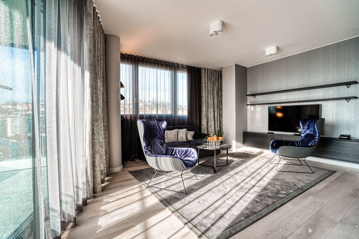 Uma sala de estar moderna com um sofá, duas poltronas, uma mesa de centro e uma TV fixada na parede.
