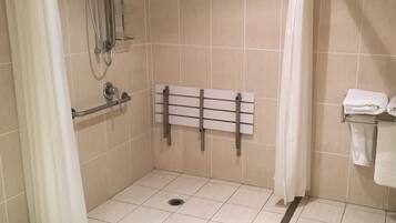 Pequeno espaço de duche revestido a azulejos, com barra de apoio, suporte para toalhas e cortina de chuveiro.