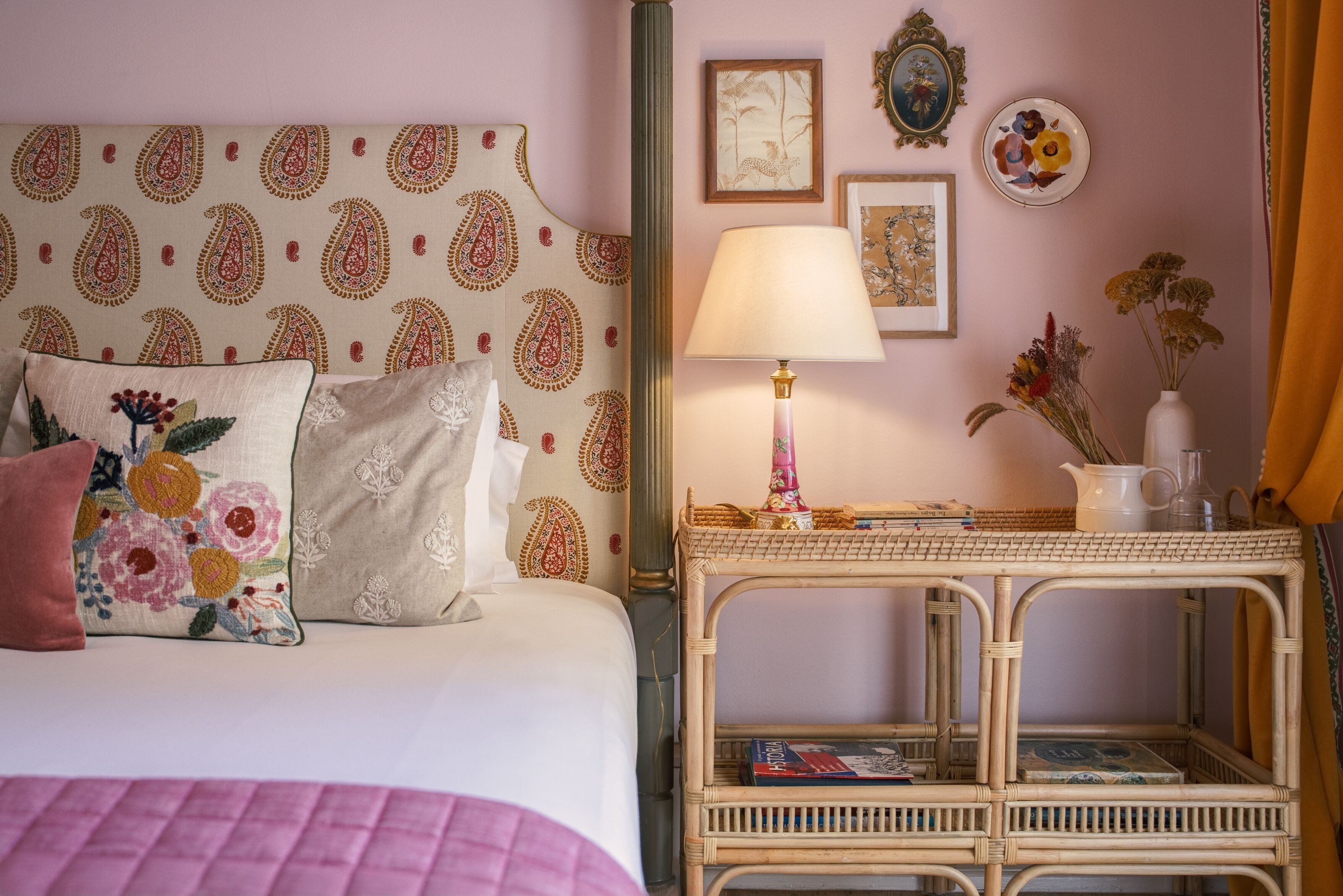 Quarto bem arrumado com cabeceira estampada, mesa de cabeceira com abajur e objetos decorativos na parede.
